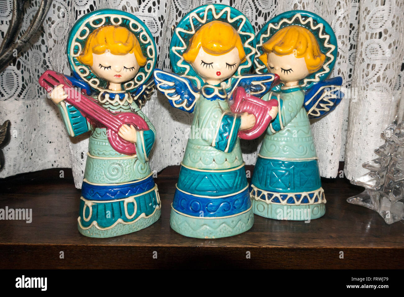Three figurine angels playing instruments on shelf with lace curtain ...