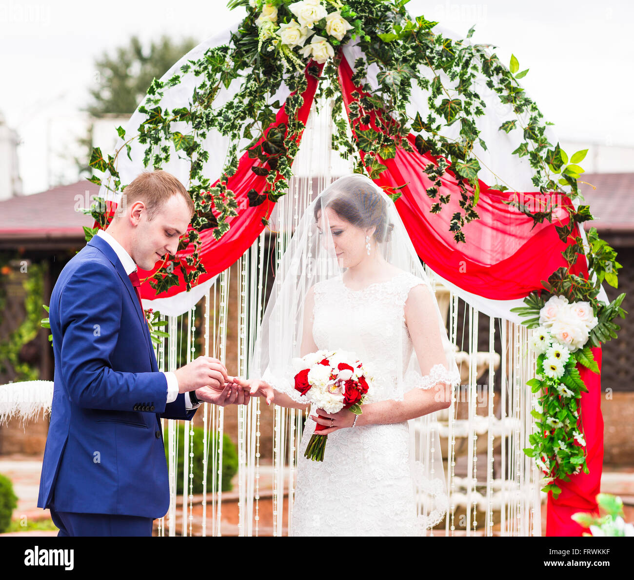 couple in wedding attire exchange rings with arch on background Stock ...