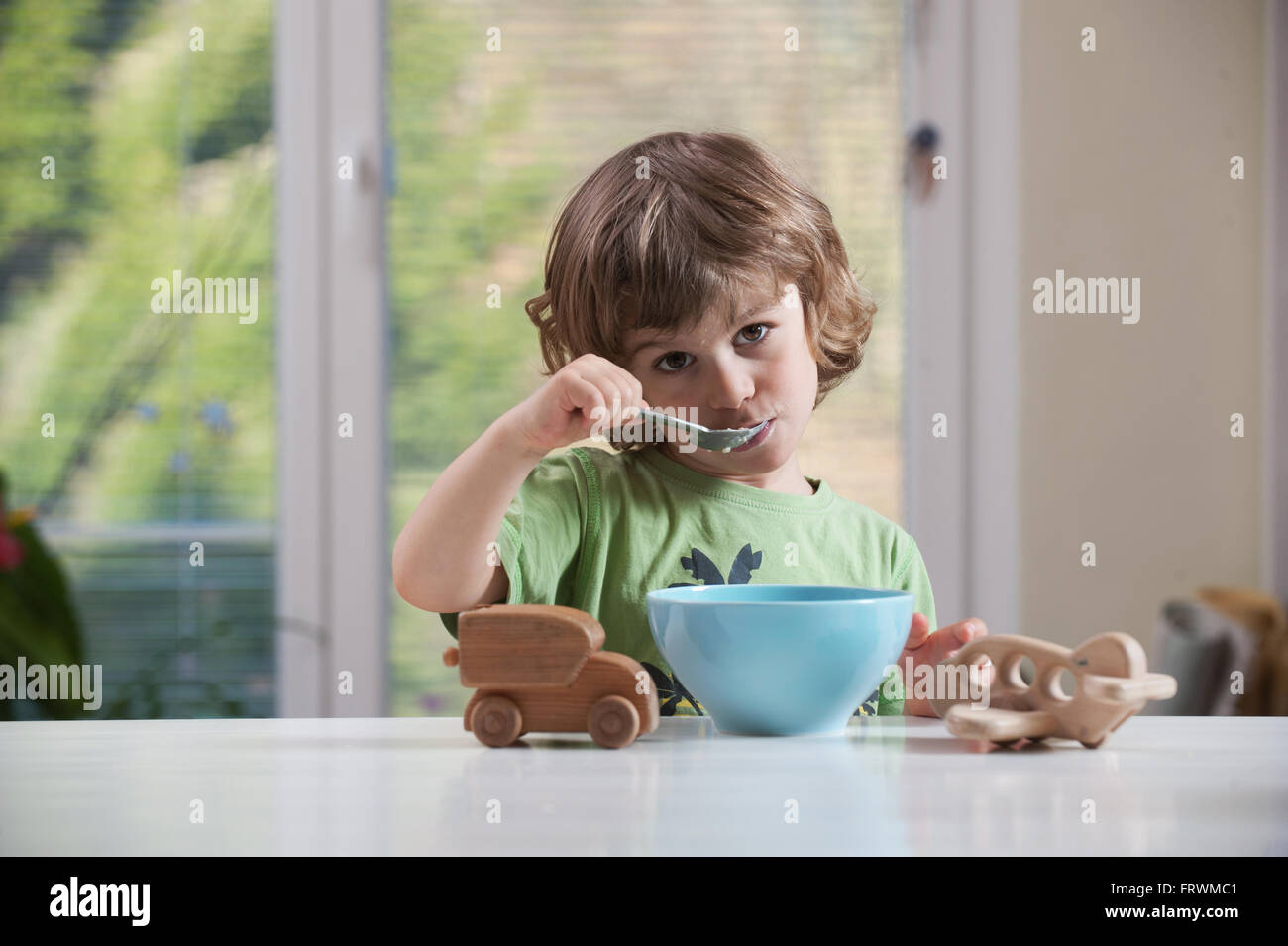 Cute little boy eating his meal while playing with toys Stock Photo - Alamy
