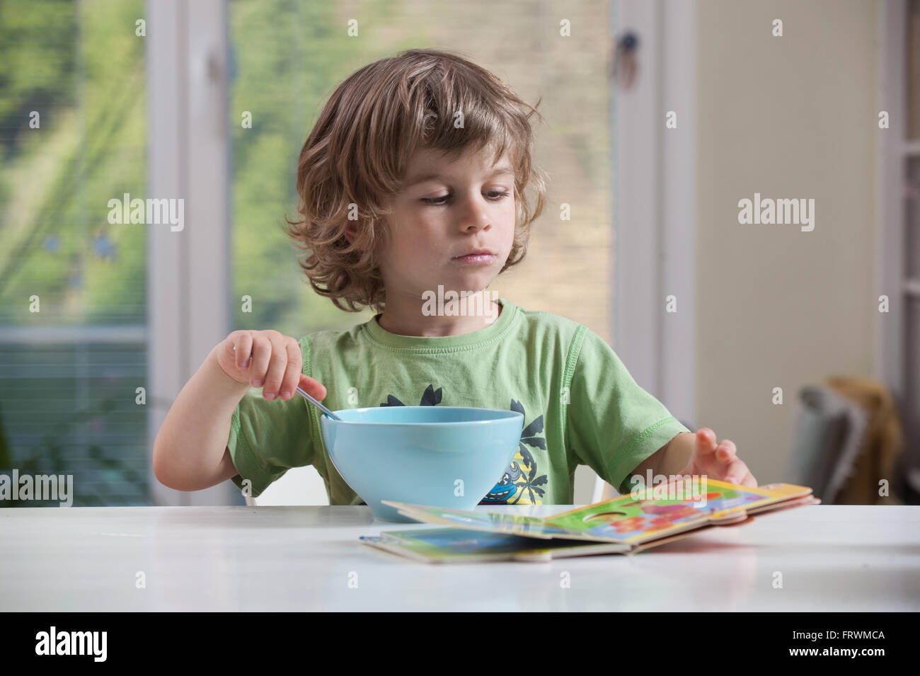 Cute little boy eating his meal while playing with toys Stock Photo - Alamy