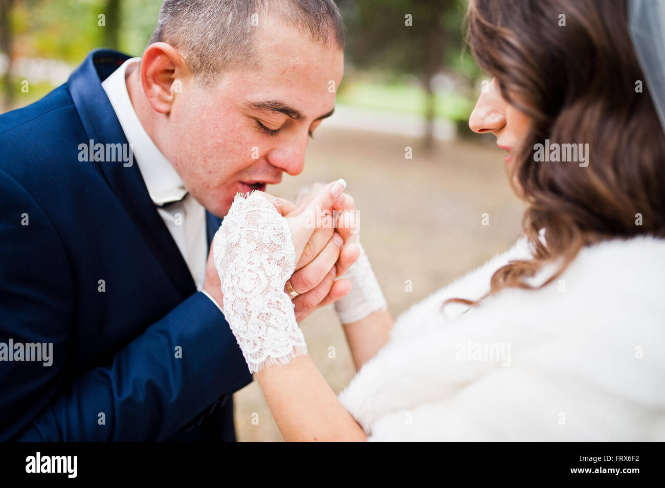 Close up portrait of kissing wedding couple, groom kiss hands of bride ...