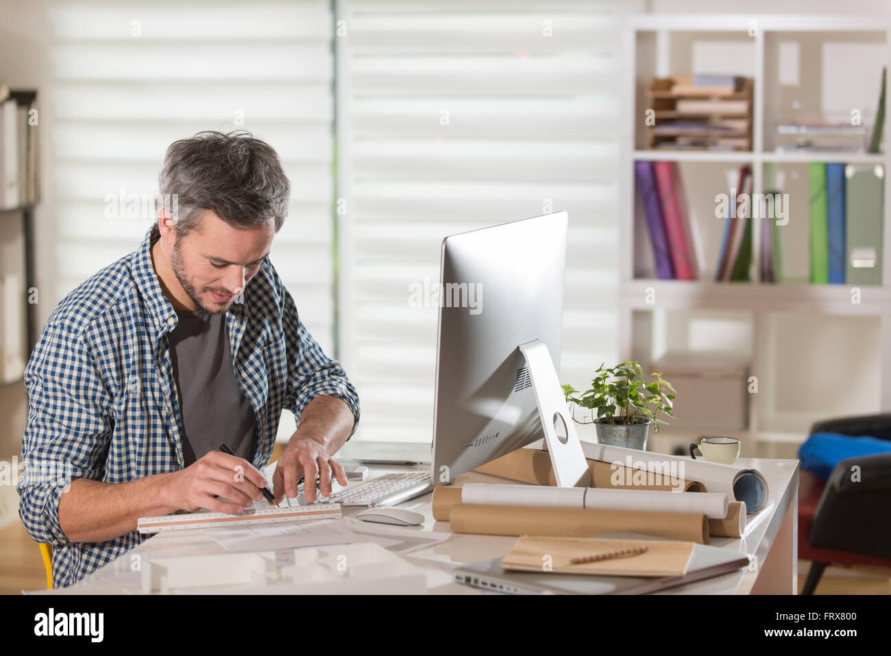 Gray haired architect wearing beard, sitting at office and working on a ...