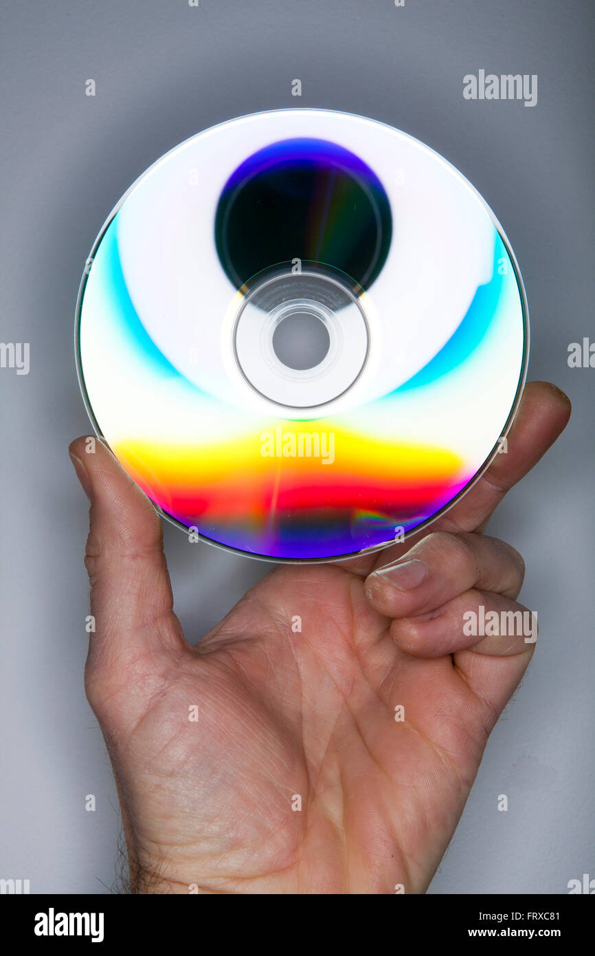 A hand holding up a DVD or CD shwoing the rainbow colours on the data ...