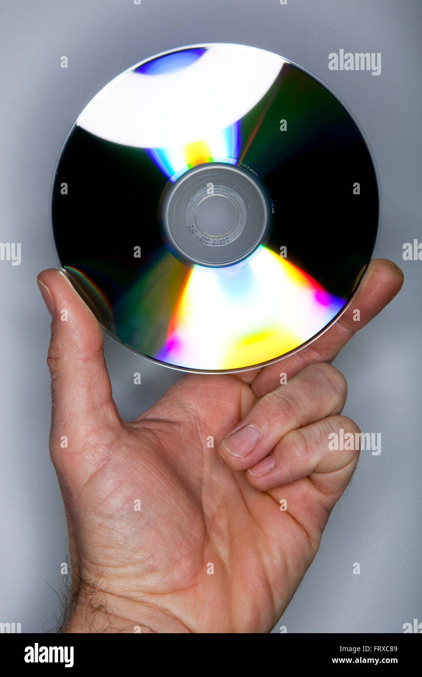 A hand holding up a DVD or CD shwoing the rainbow colours on the data ...