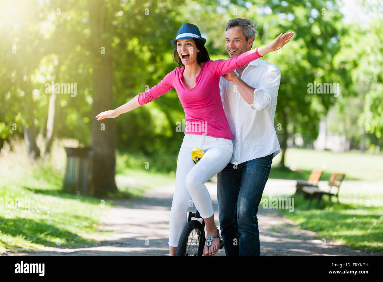 A lovely couple is having fun on a unicycle in the park. A beautiful ...
