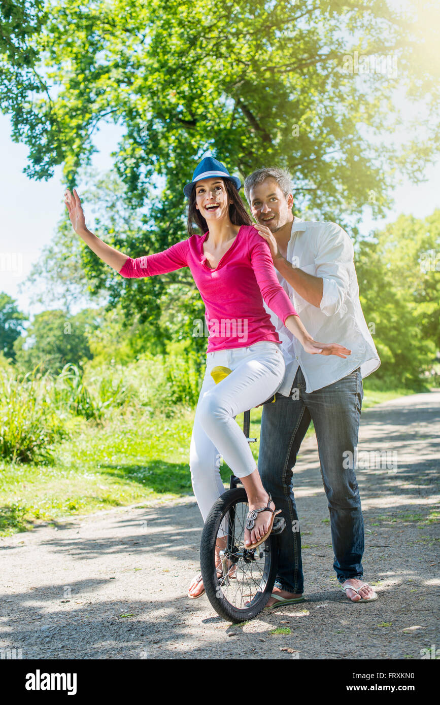 A lovely couple is having fun on a unicycle in the park. A beautiful ...