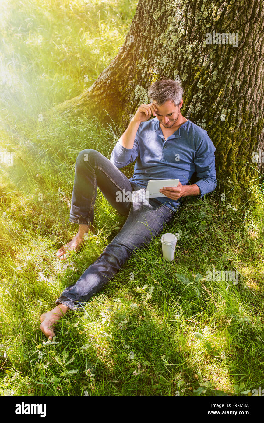 A nice looking grey hair man is sitting against a tree in the grass ...