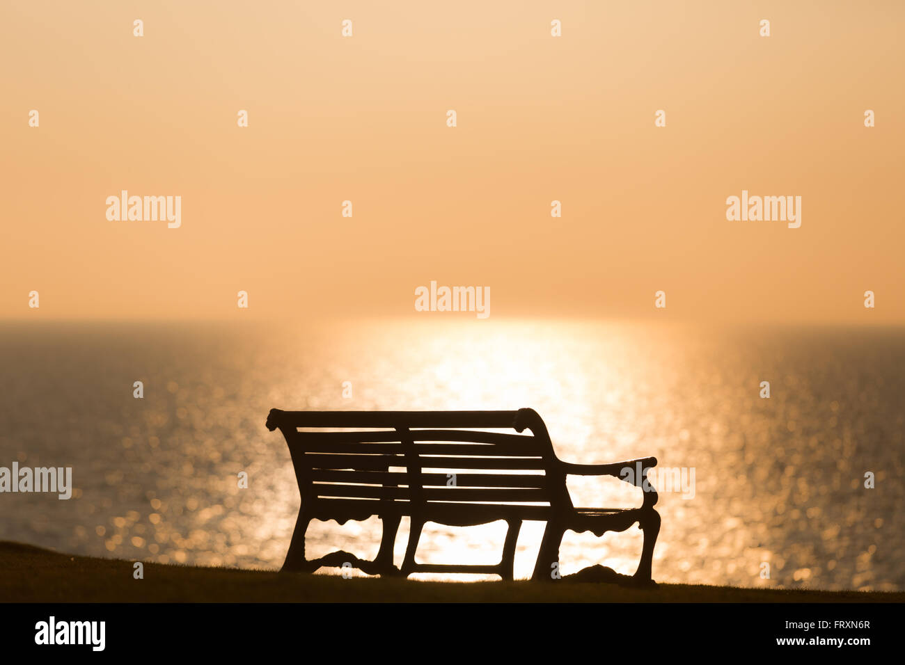 A bench facing out to sea with the sun reflecting across the water ...