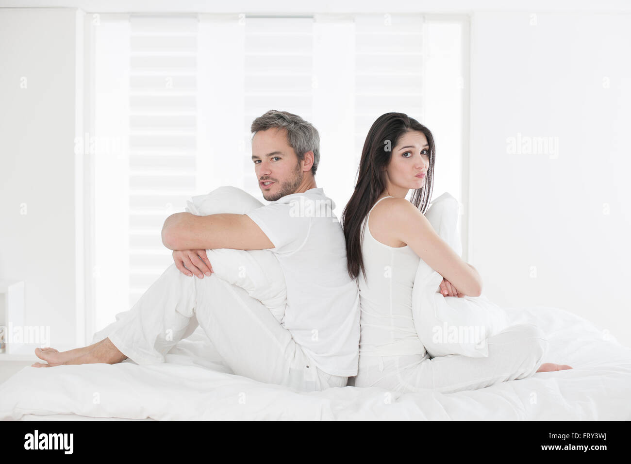 Unhappy Couple Ignoring Each Other Sitting Back To Back On Bed During A