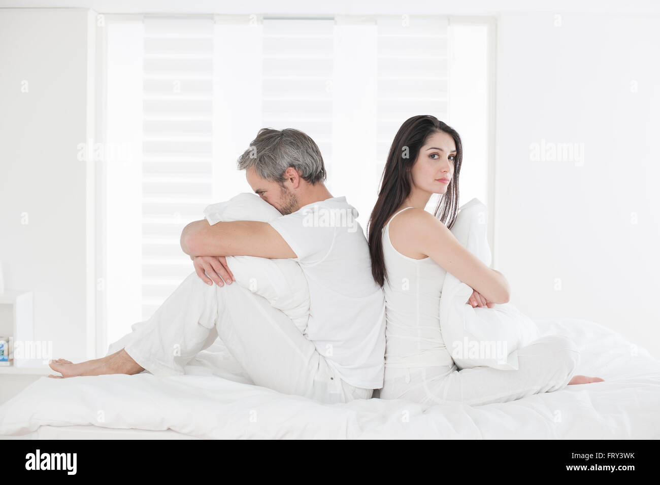 Unhappy Couple Ignoring Each Other Sitting Back To Back On Bed During A