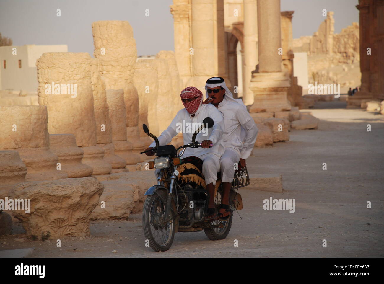 Two men on a moped pass the ruins of the ancient city of Palmyra in the ...