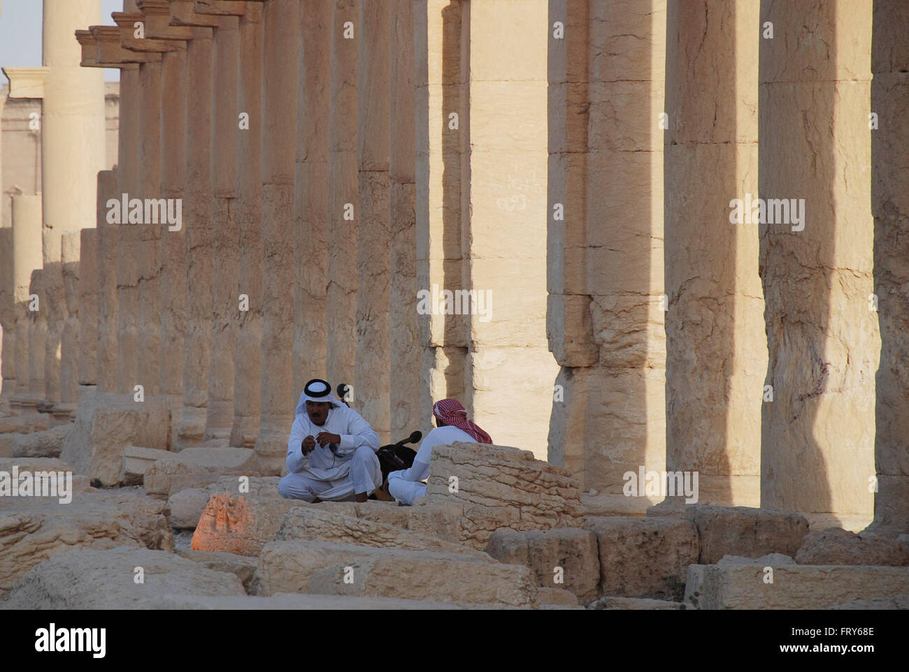 Two men sit among the ruins of the ancient city of Palmyra in the ...
