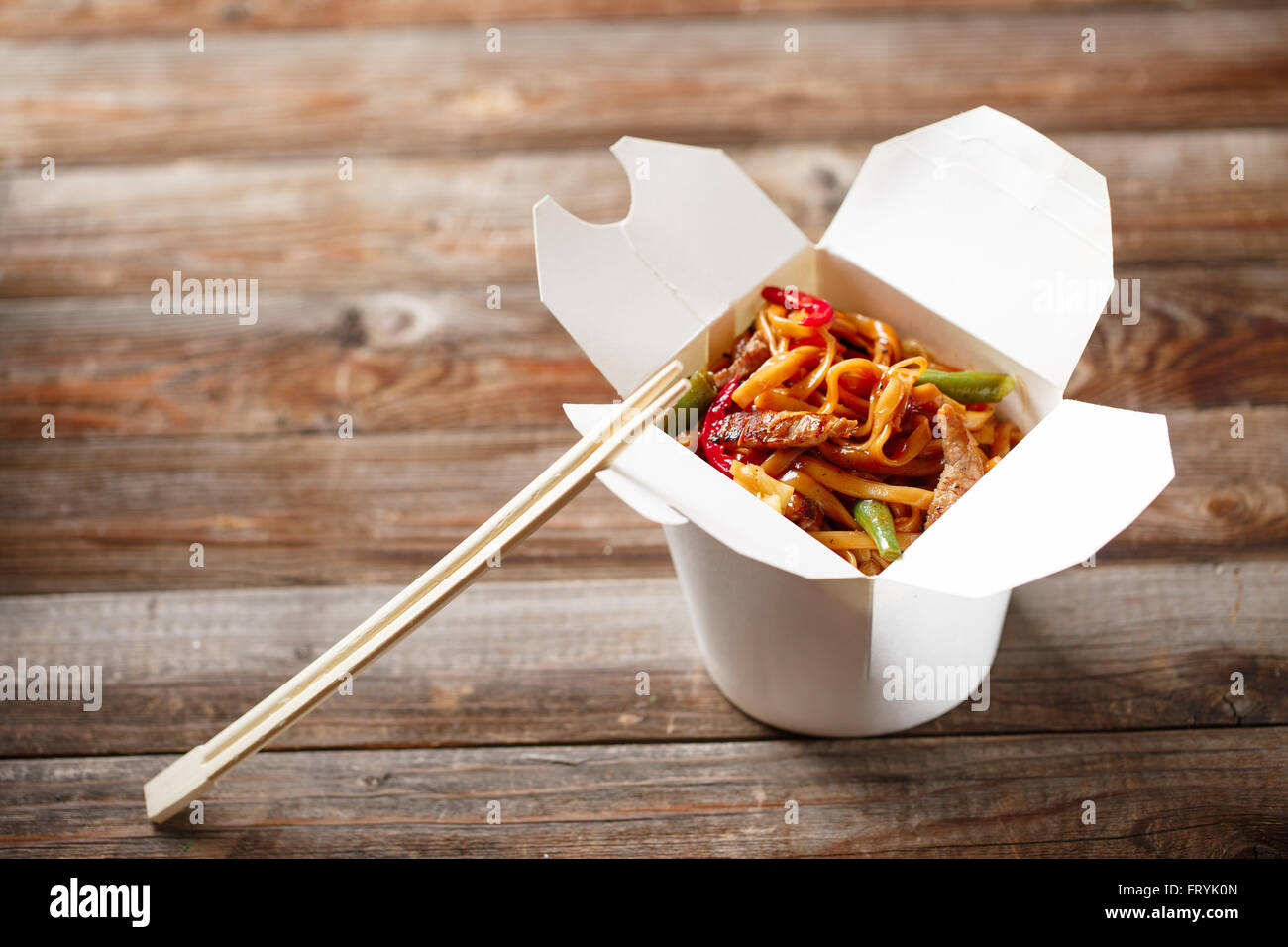 Noodles with pork and vegetables in take-out box on wooden table Stock ...
