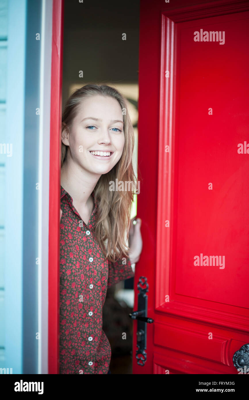 beautiful young woman opening a red door to welcome someone Stock Photo ...