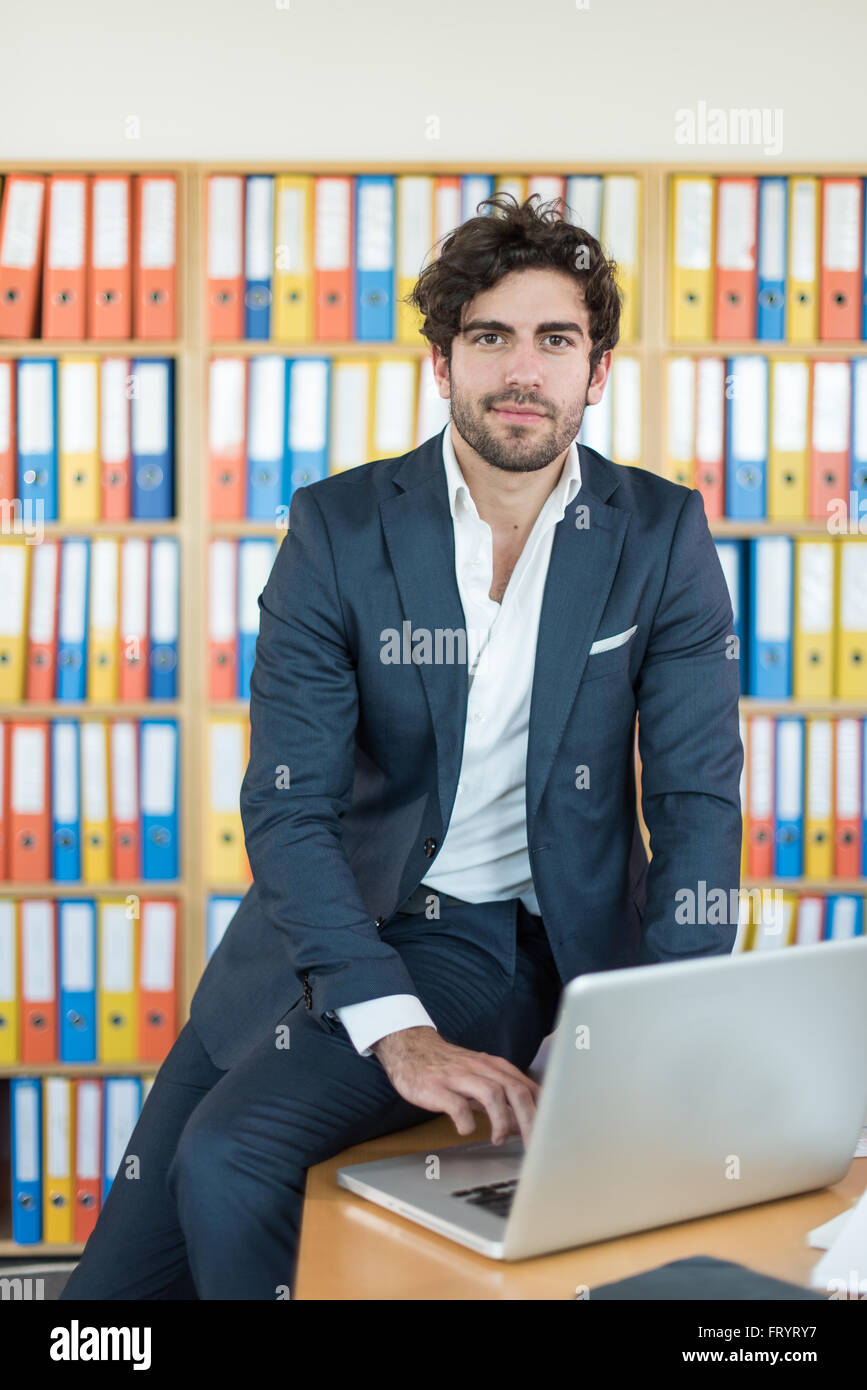 Portrait of a stylish executive sitting on the desk in front of a ...