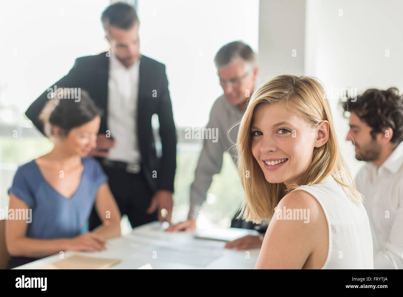 Portrait of a smiling blond assistant, she is turned back on her chair ...