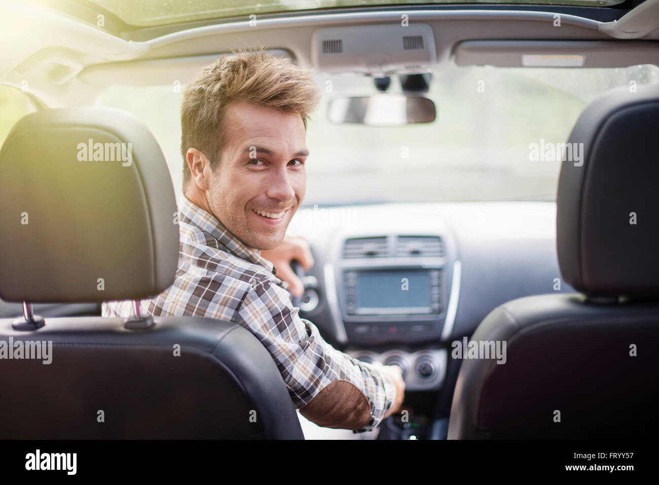 handsome man looking at camera sitting in a car, view from rear seat ...