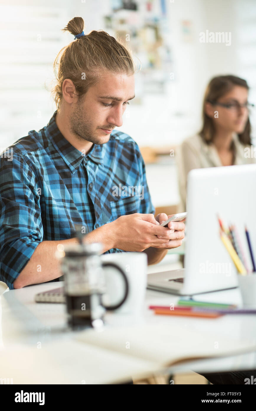 portrait of a young man at his computer and using a phone, at the ...