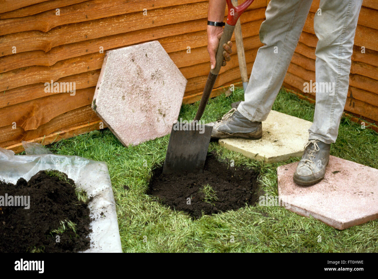 Close-up of a gardener digging out turf before laying hexagonal paving ...
