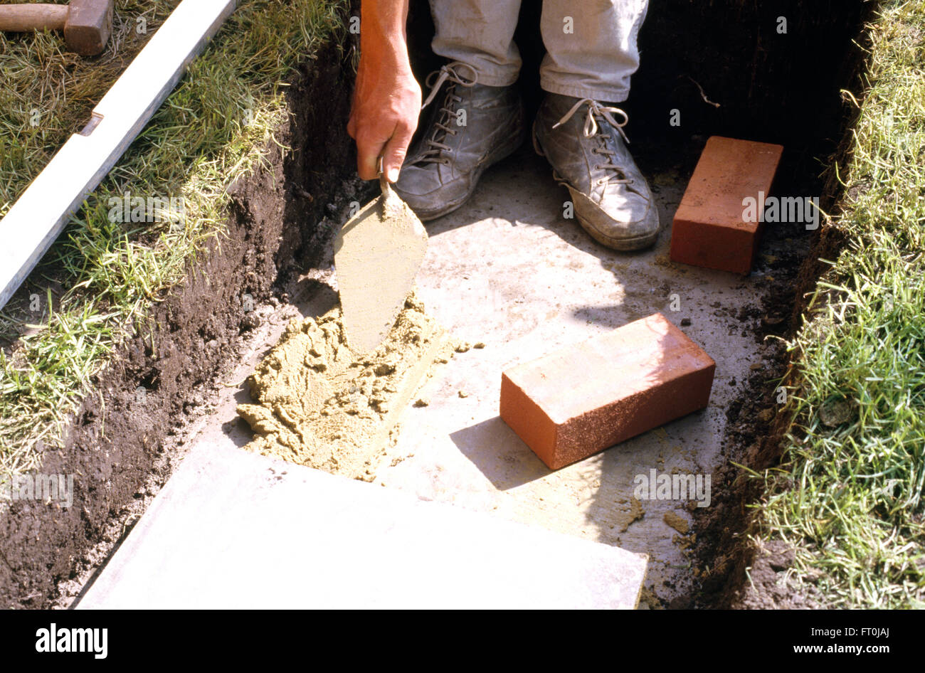 Close-up of a workman applying cement to the base of a shallow trench ...