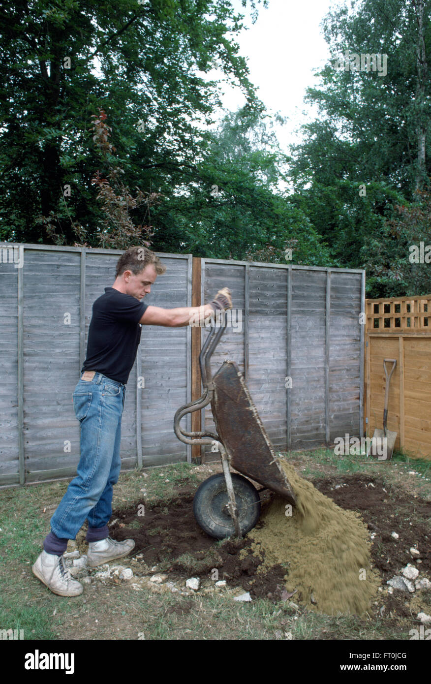 Gardener tipping sand from a wheelbarrow onto a new rockery area FOR ...