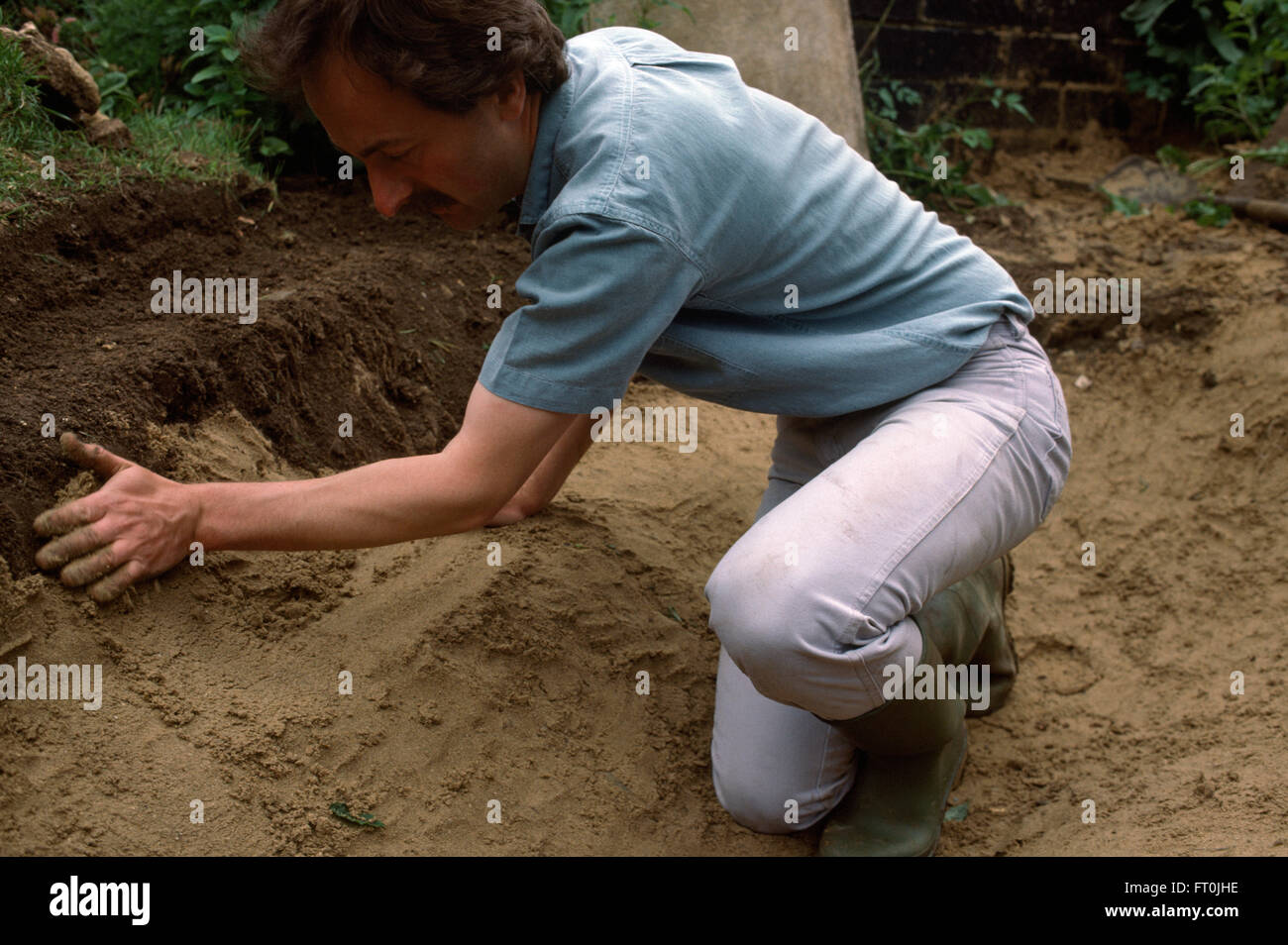 Close-up of a man tamping down sand in newly dug area for a new pond ...