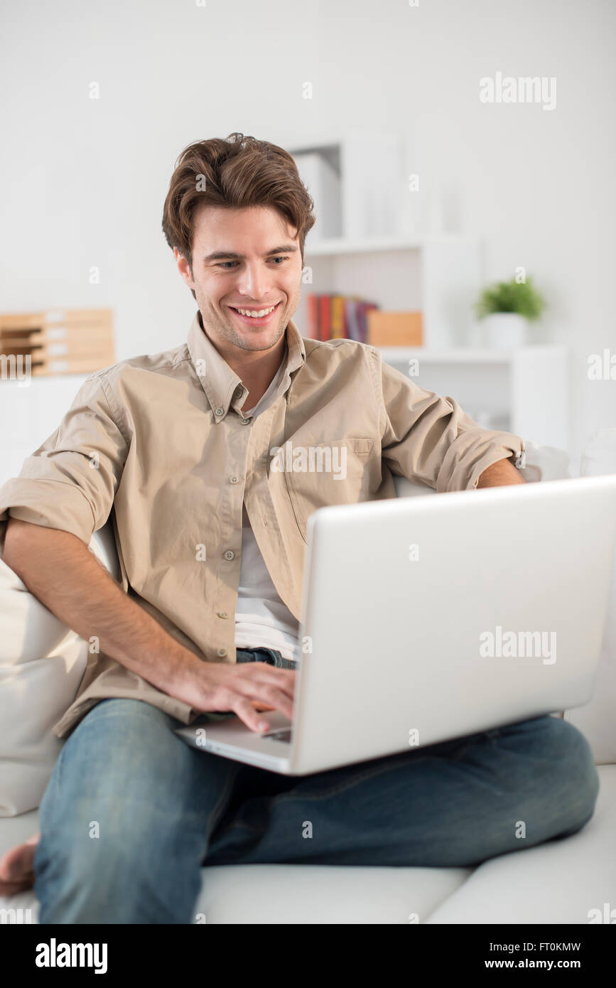 Handsome man sitting on a couch using a laptop Stock Photo - Alamy