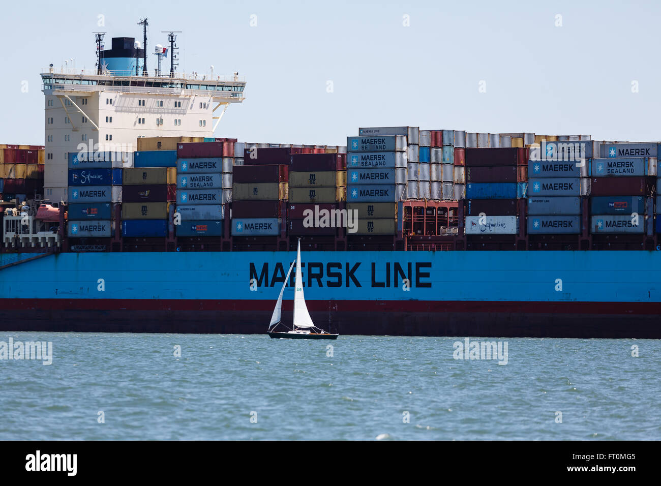 Sailboat next to container cargo ship looks very tiny against its side ...
