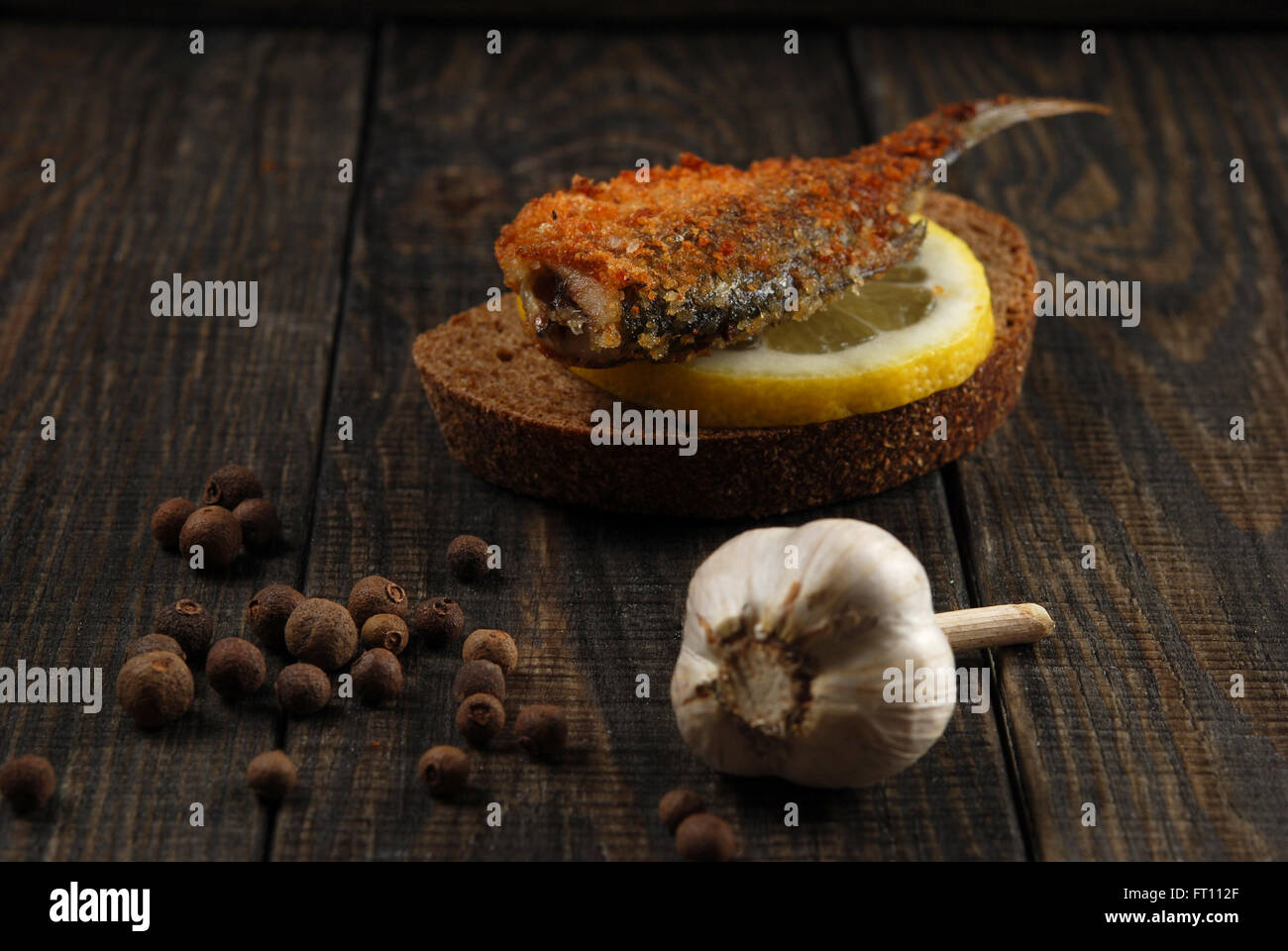 sandwich of rye bread with fried fish and lemon on a wooden background ...