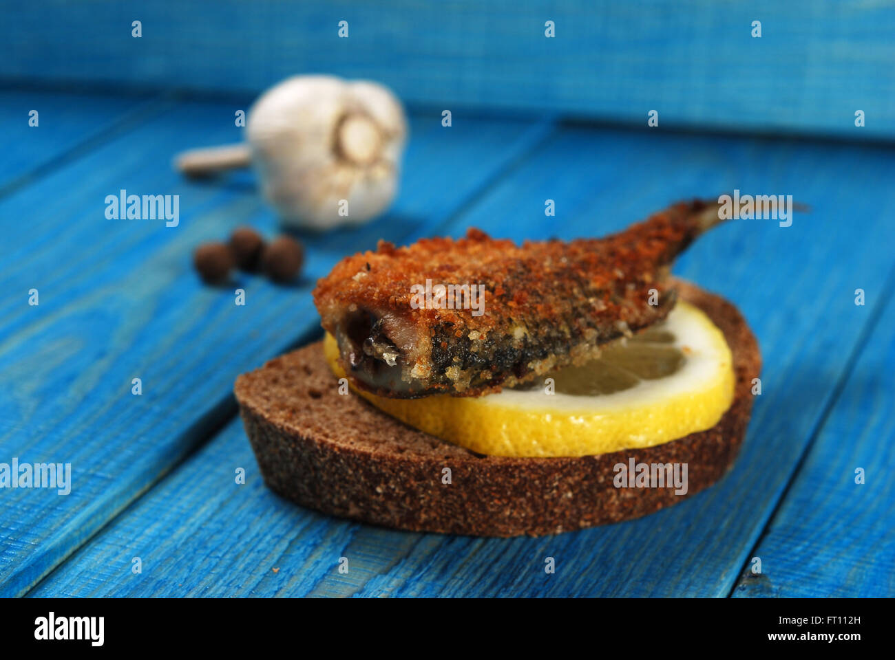 sandwich of rye bread with fried fish and lemon on a blue wooden ...