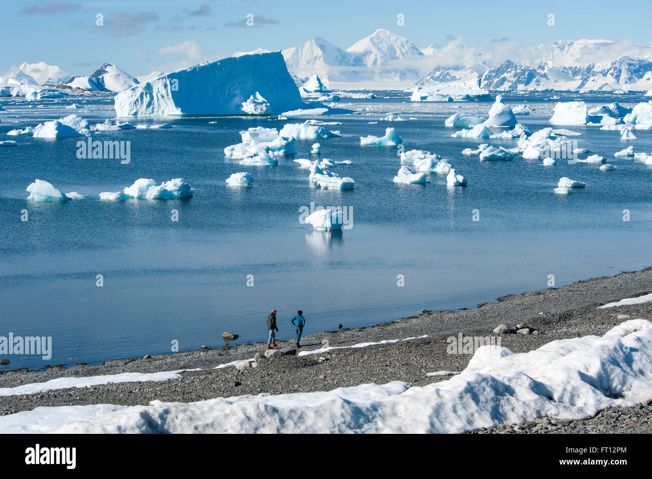 People walking along the rocky beach near Rothera Station with icebergs ...