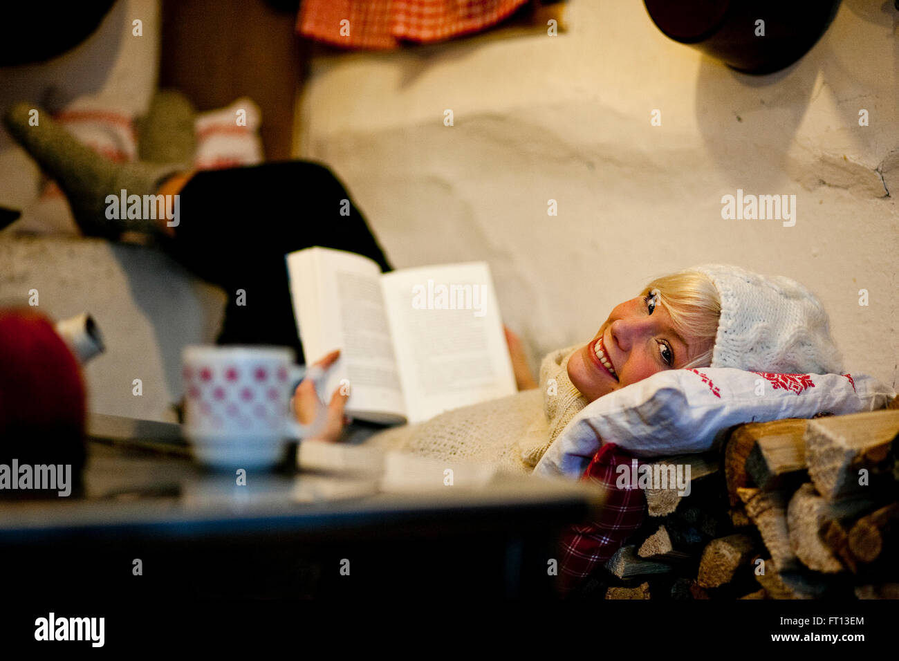 Young woman reading a book while lying on a fireside bench Stock Photo ...