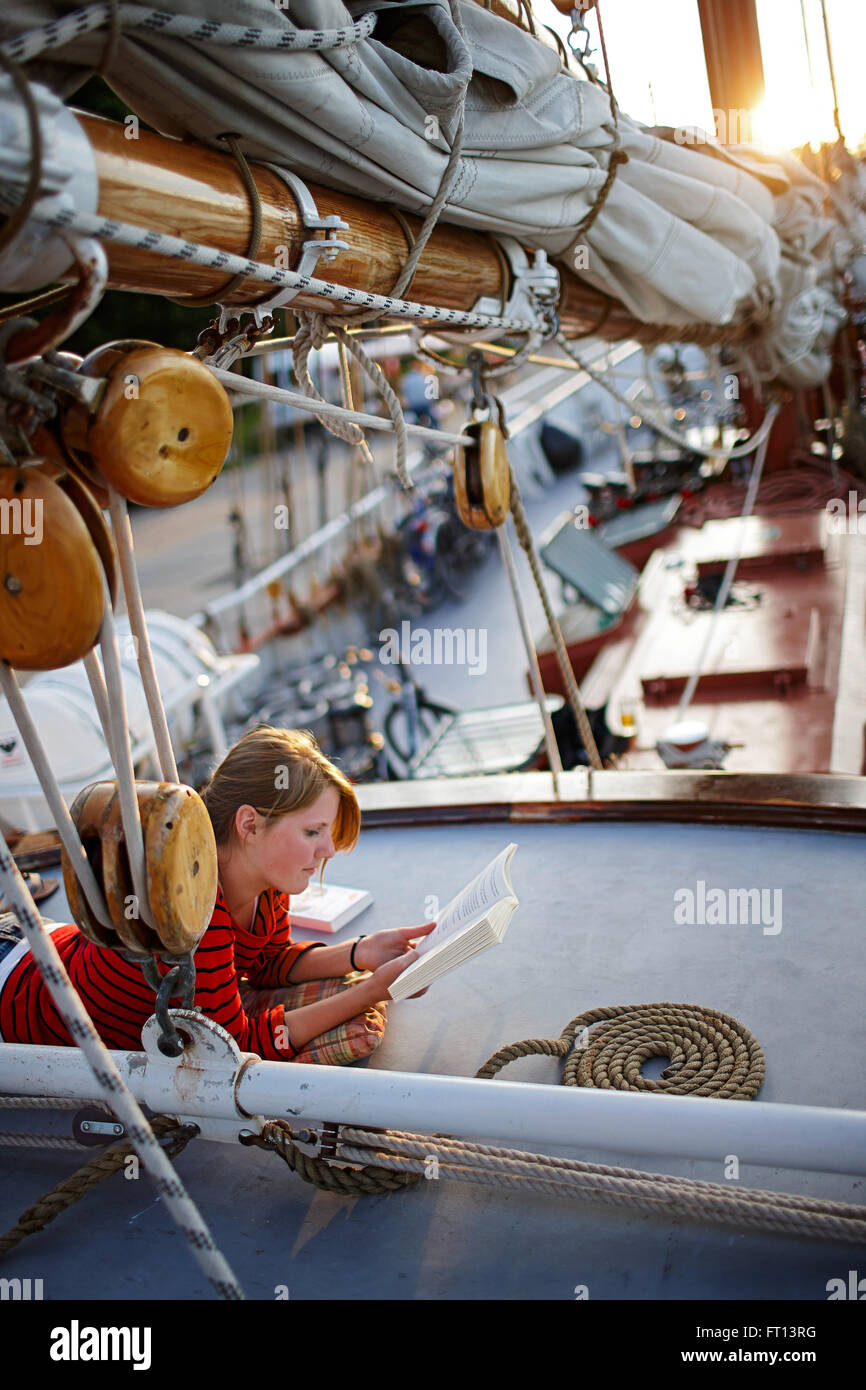 Teenager lying on deck of sailing ship while reading a book, Lauterbach ...