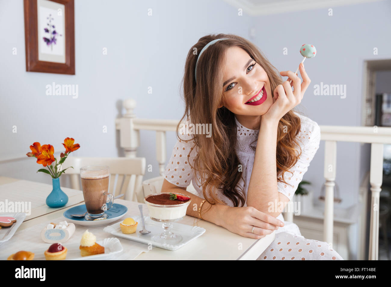 Cheerful pretty young woman sitting and eating lollipop in cafe Stock ...