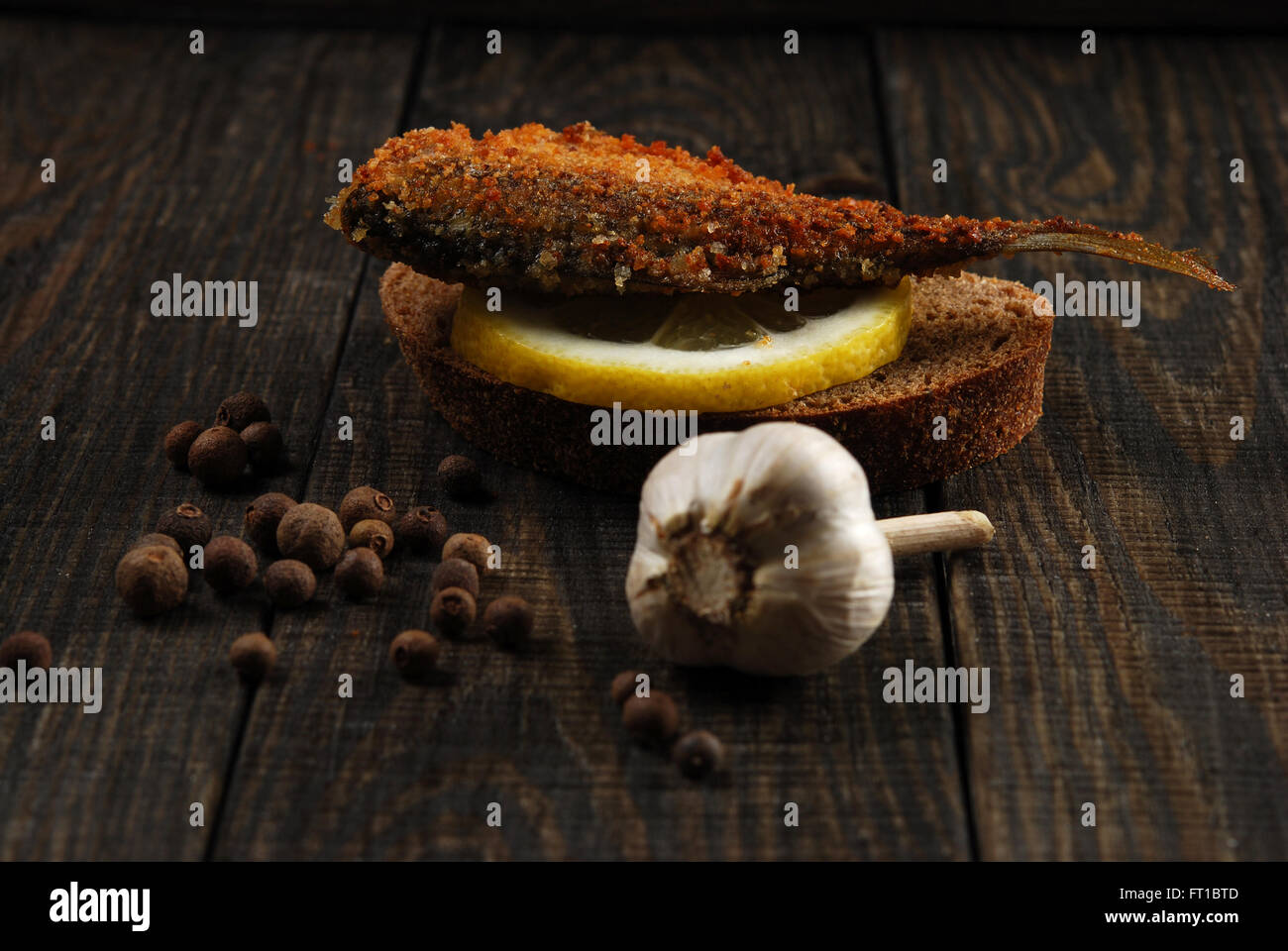 sandwich of rye bread with fried fish and lemon on a wooden background ...