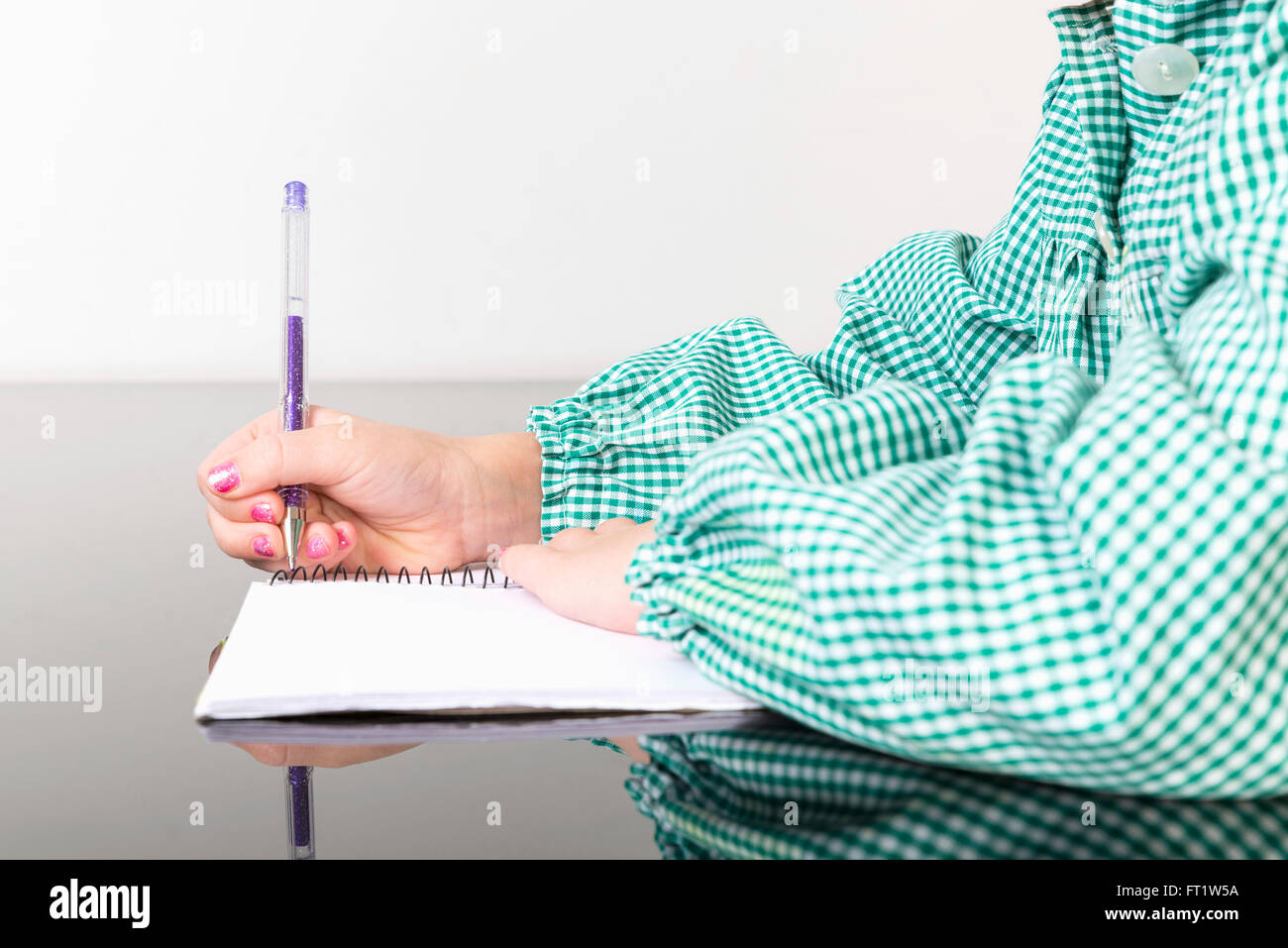 Little girl with a green plaid smock writing in a notebook at home ...