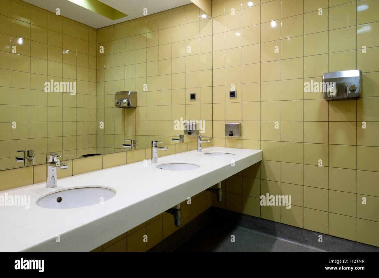 Public restroom with a row of lavatories in front of a large mirror ...