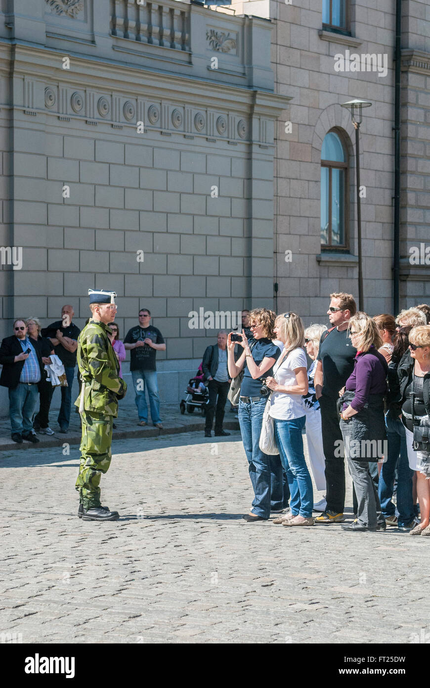 People waiting in a line and observing a guard dressed in green uniform ...