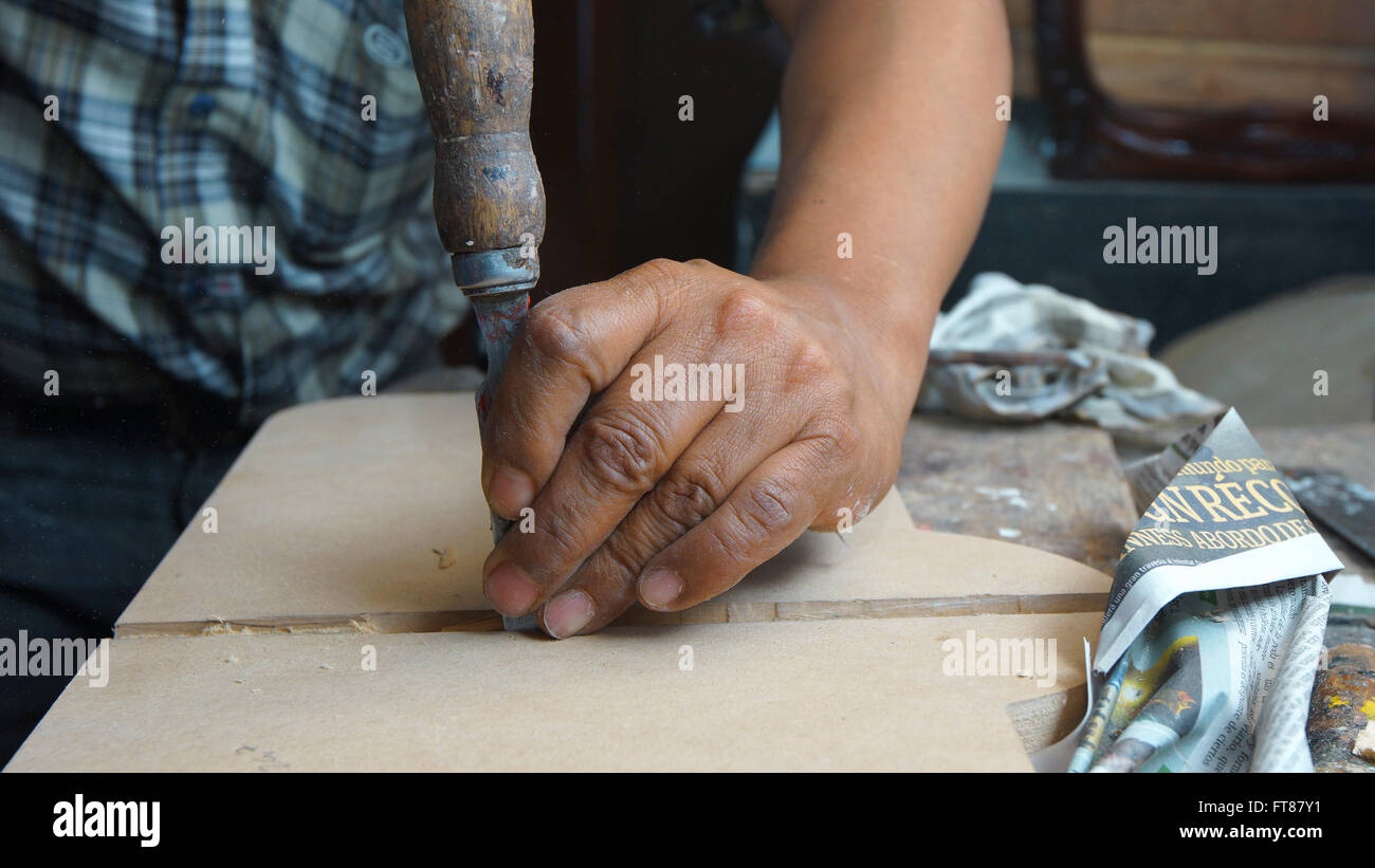 Carpenter's hand holding a chisel modeling a wooden board on his desk ...