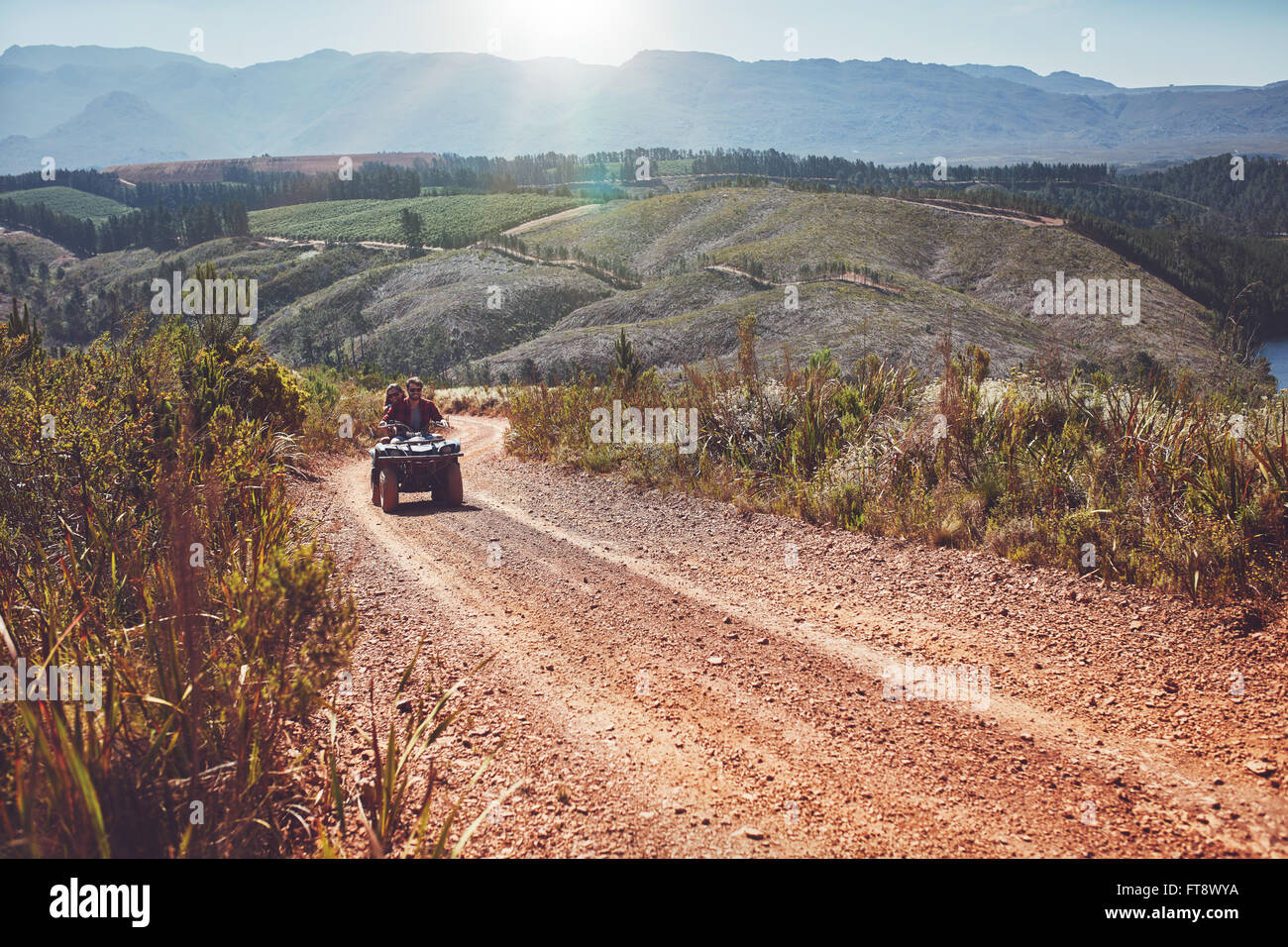 View of a couple driving an ATV on dirt road in countryside. Young man ...