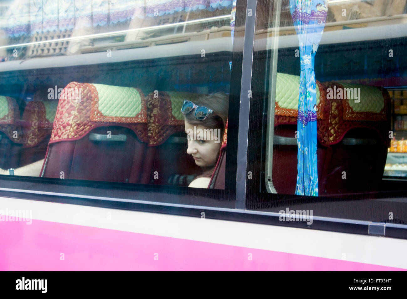 A woman bus passenger is looking through a window on a bus on a street ...