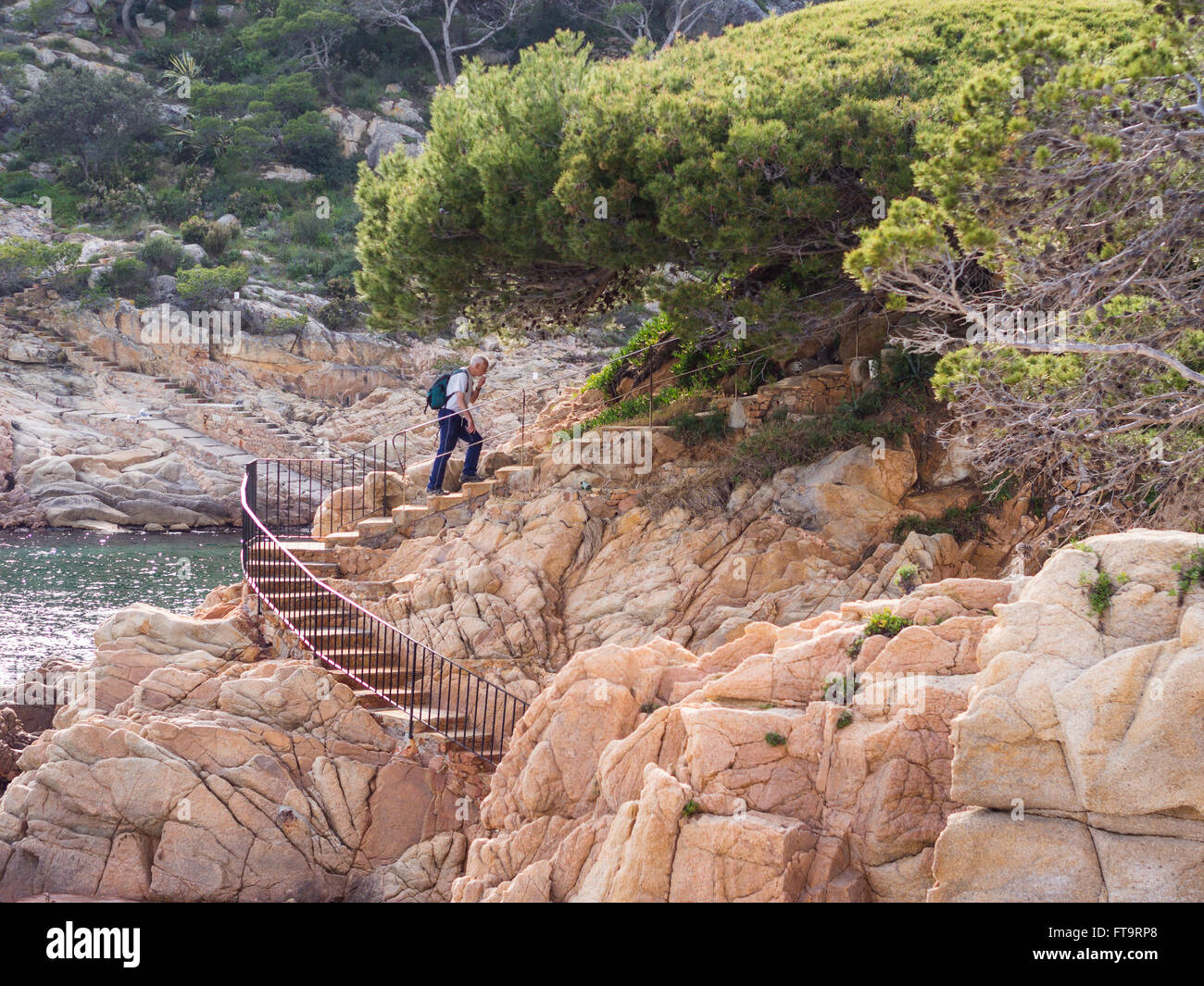 Walking the Coastal Path GR82. A man walks up stairs built into the ...