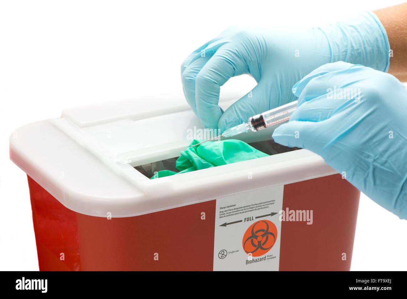 Health care worker's gloved hand drops syringe into hazardous waste ...