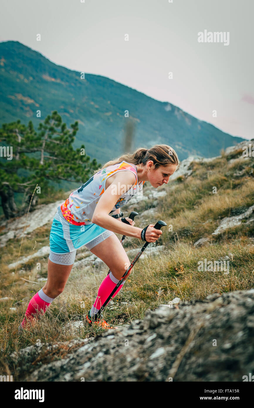 girl athlete with walking sticks going uphill during Mountain marathon ...