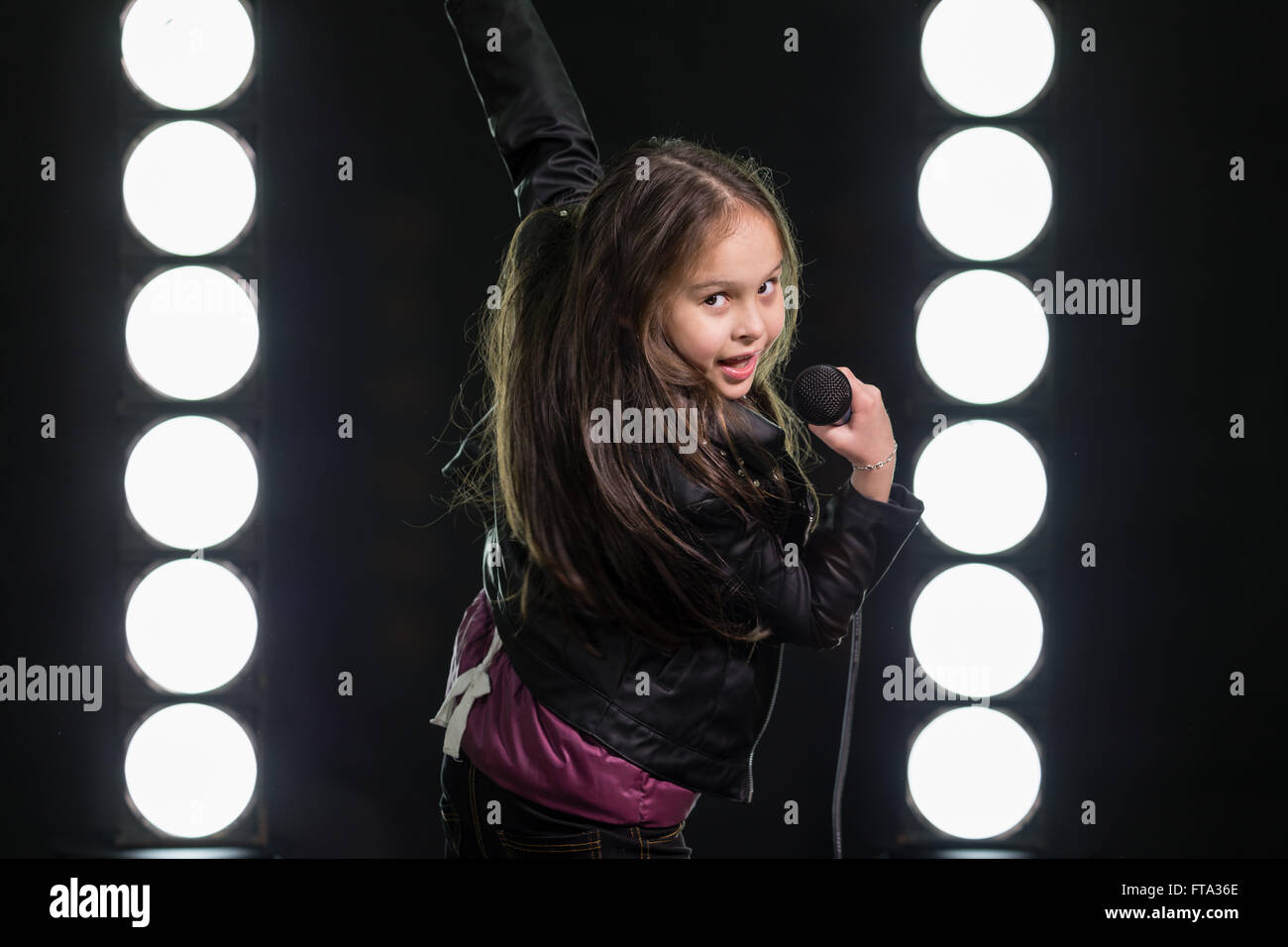 Young rockstar girl singing in front of stage lights, looking over ...