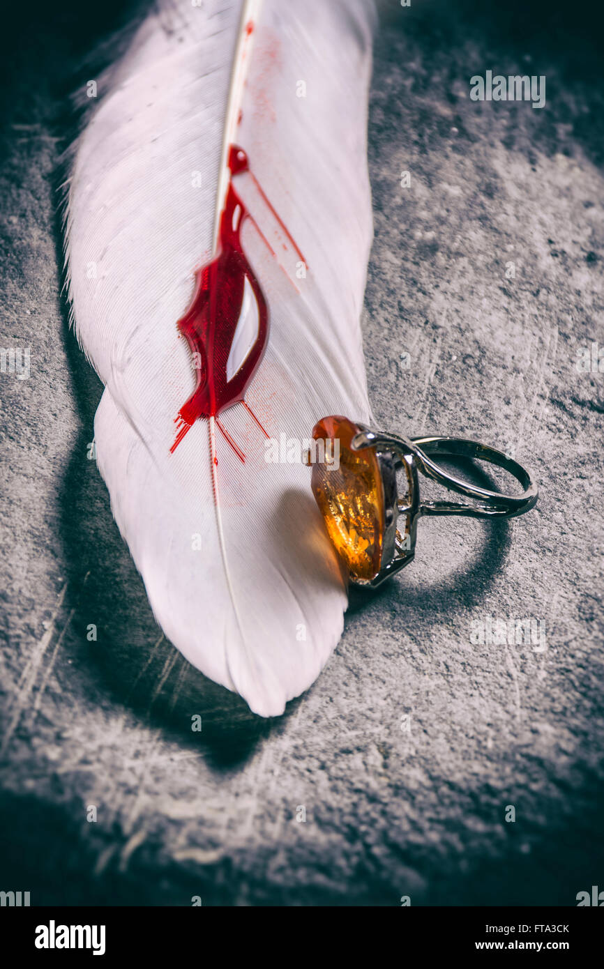 Blood on white feather with an old ring on the ground Stock Photo - Alamy
