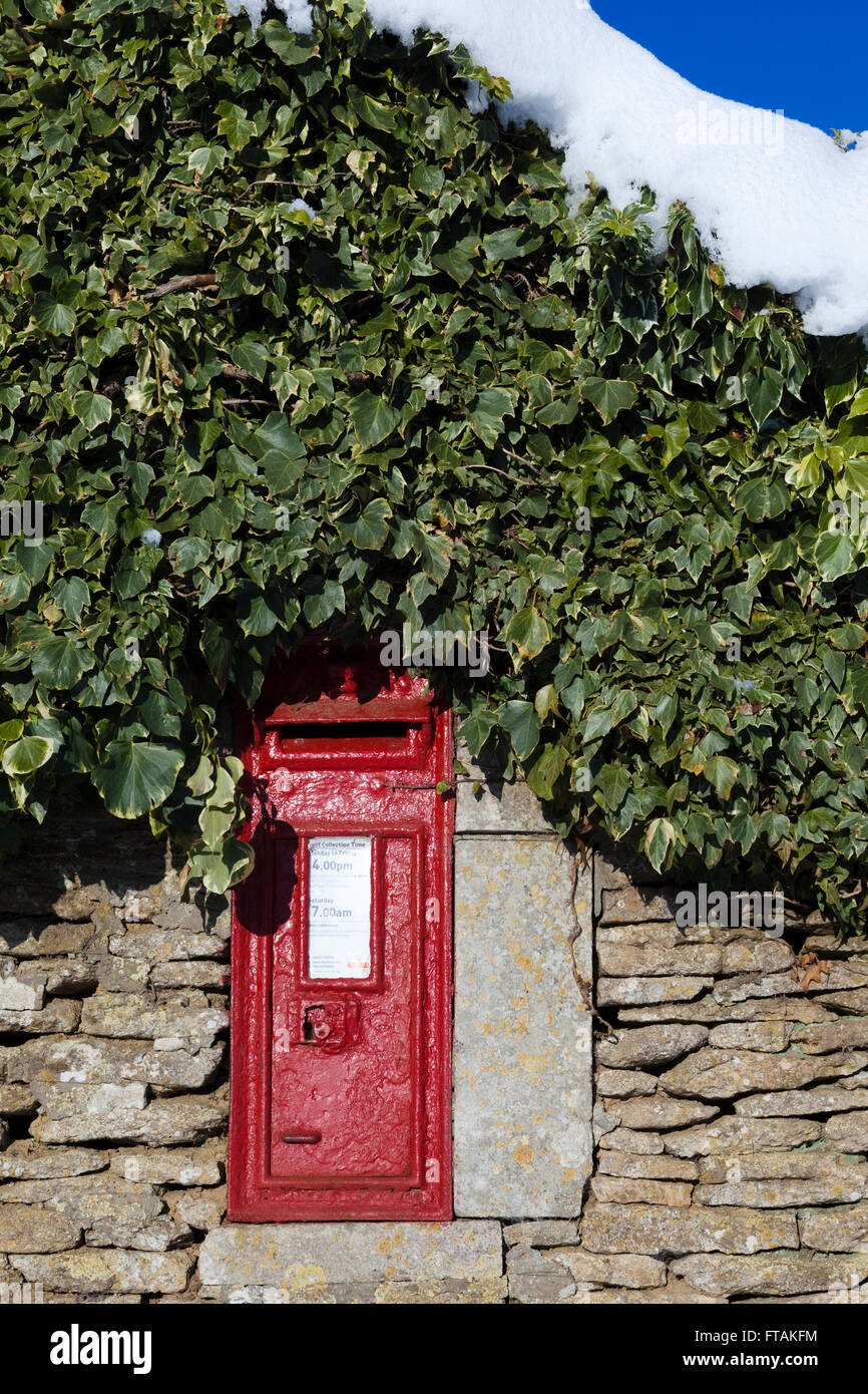 A deep red traditional post box set in a dry stone wall in the ...