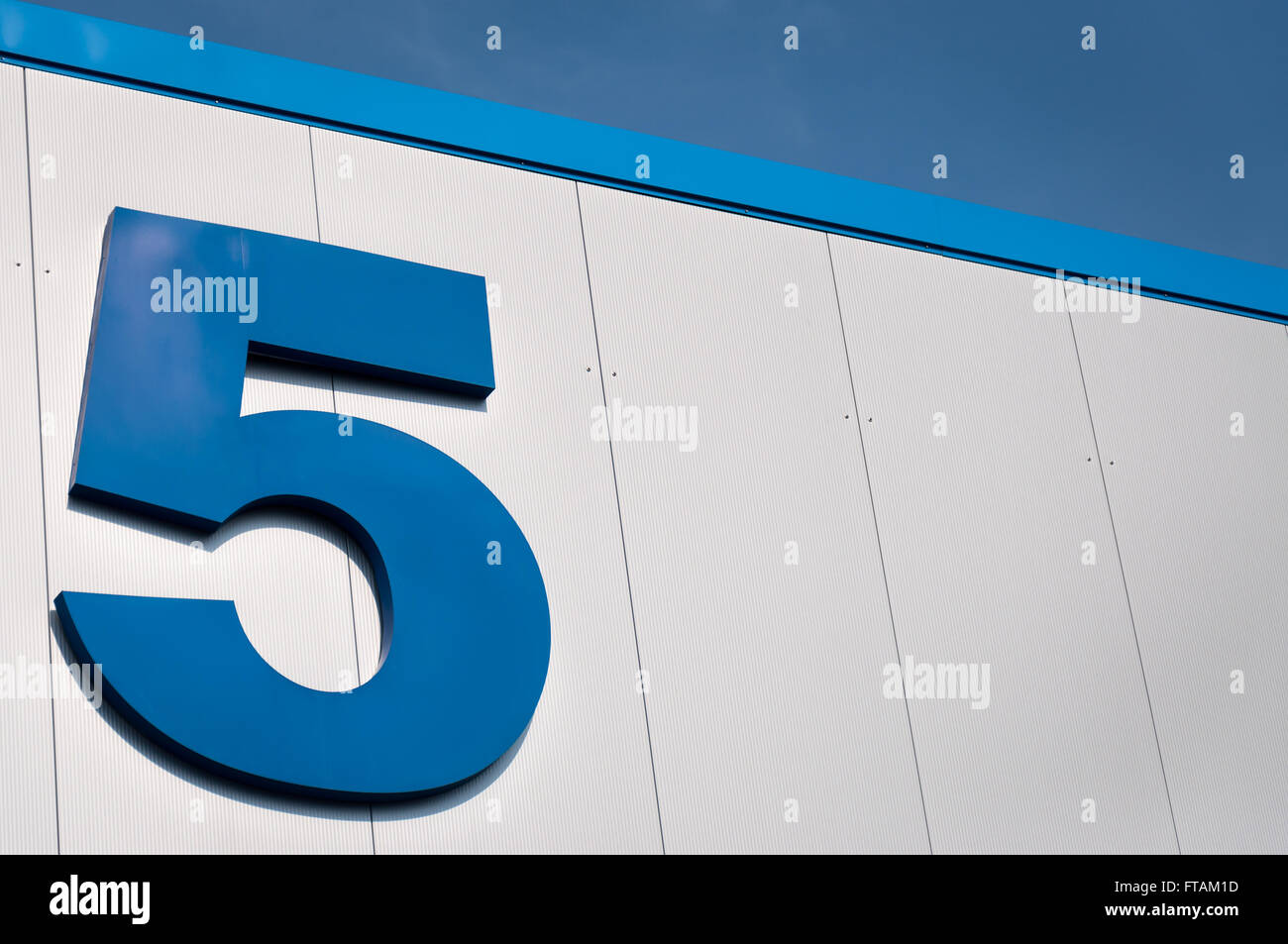 Huge blue symbol digit number 5 on white building wall against blue sky ...