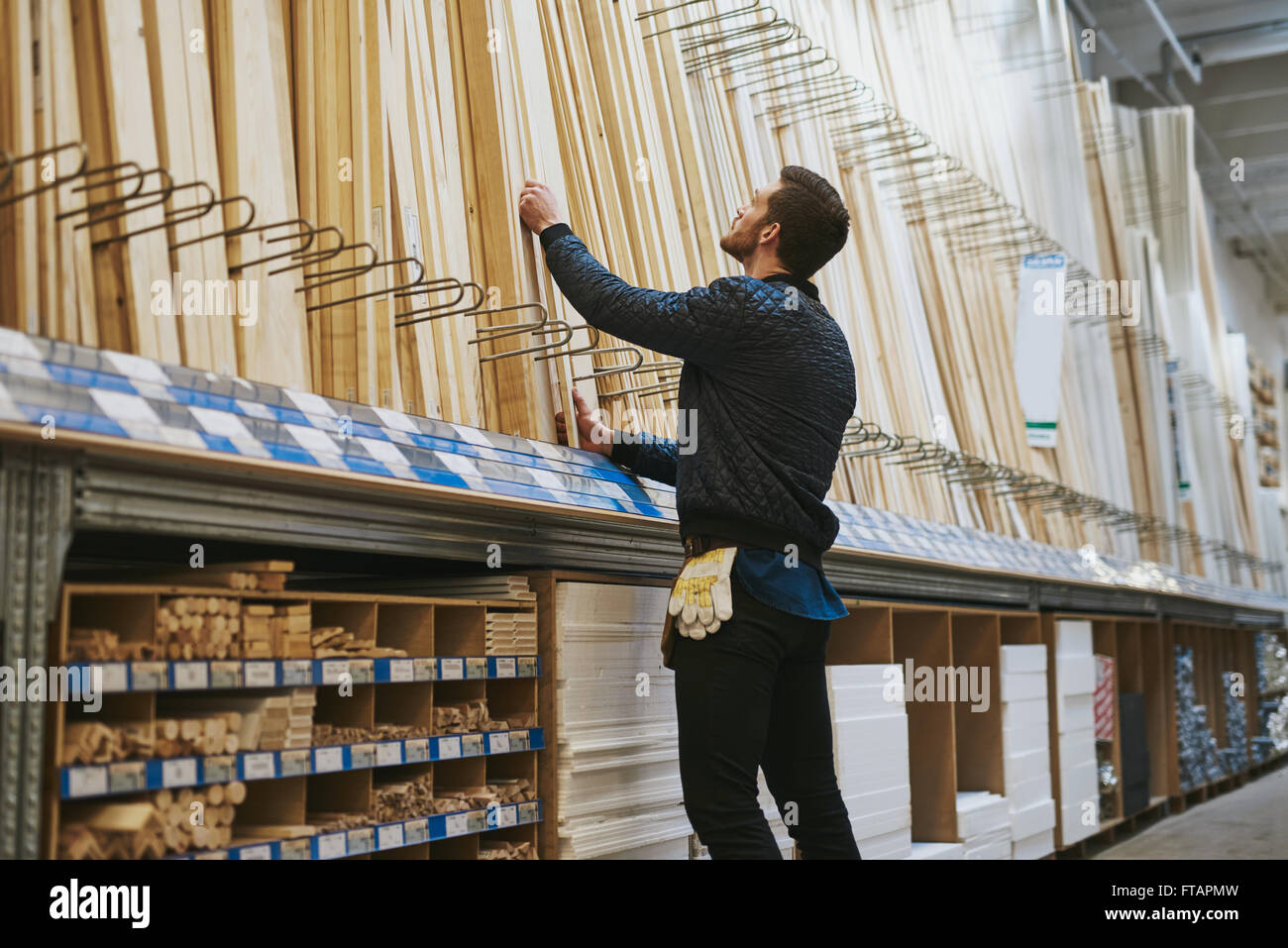 Carpenter selecting lengths of cut wood of a rack in a hardware store ...