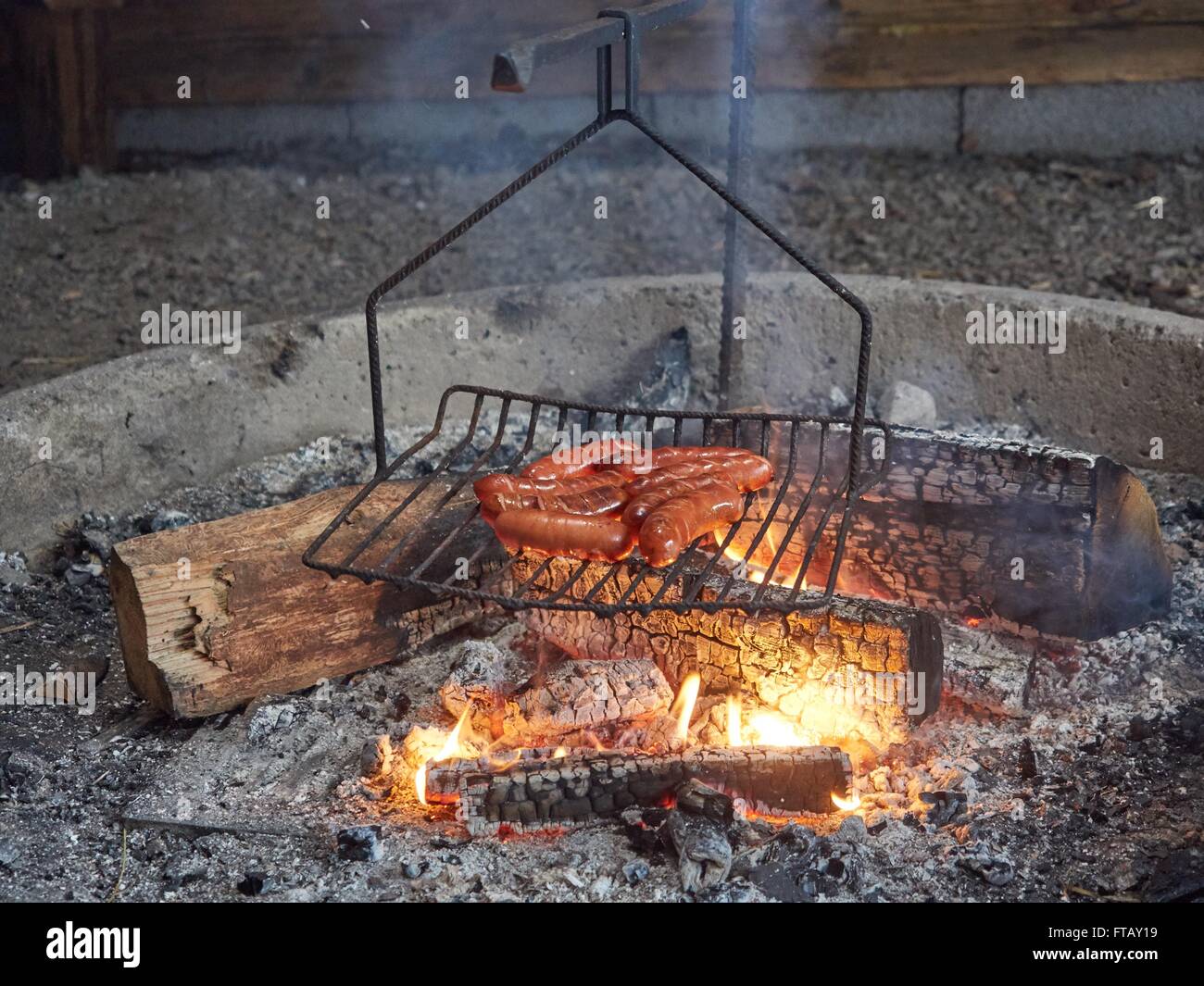Sausages hanging above campfire in a barbecue hut. Smoke rising from ...